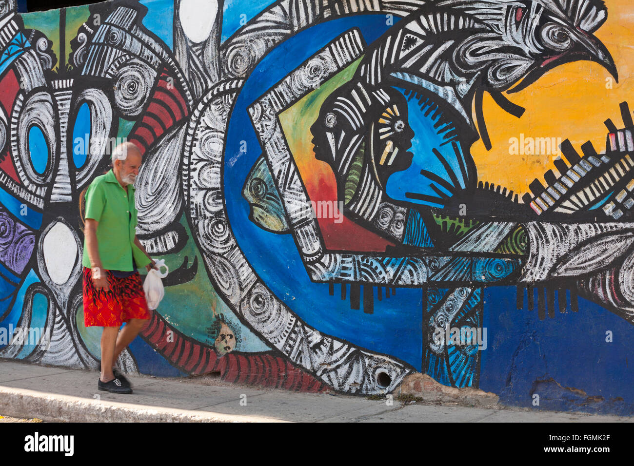 Mature Cuban man walking past Cuban artwork painted on wall at Callejon ...