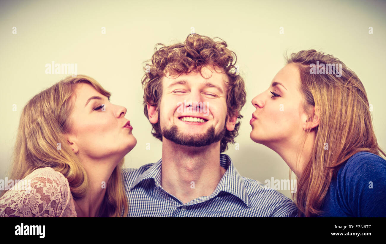 Two pretty women kissing handsome man. Love triangle Stock Photo - Alamy