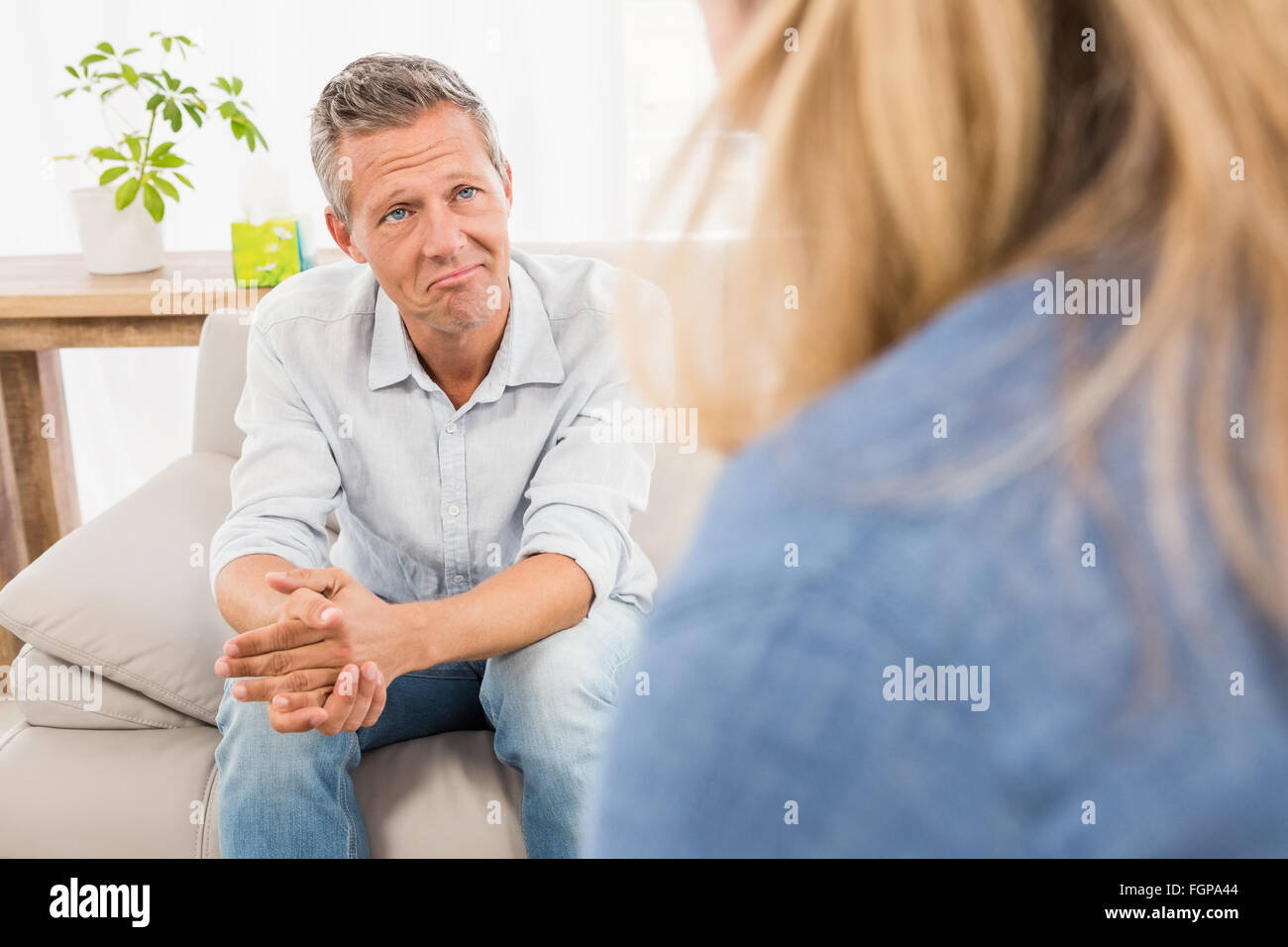 Worried man sitting on couch and talking to therapist Stock Photo - Alamy