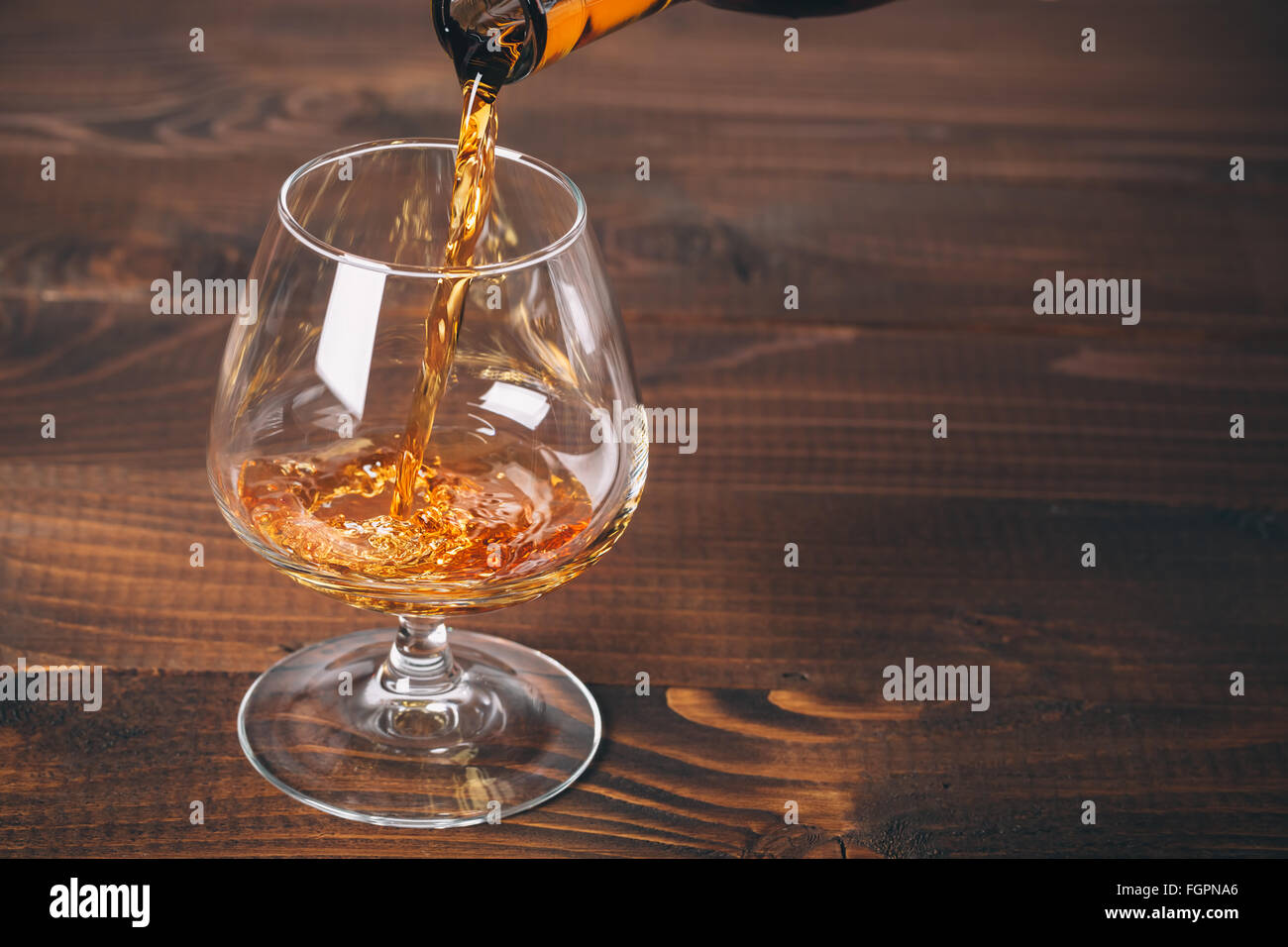 Pouring cognac or whiskey from the bottle into the glass against wooden ...