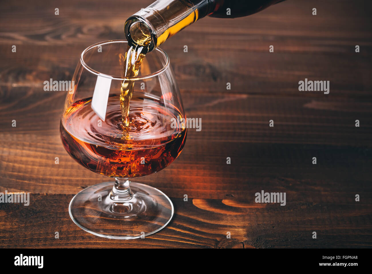 Pouring cognac or whiskey from the bottle into the glass against wooden ...