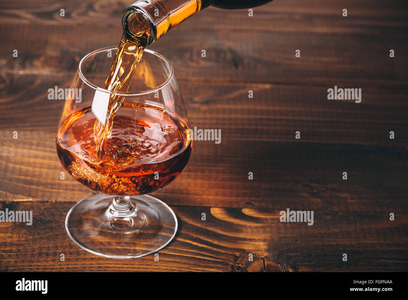 Pouring cognac or whiskey from the bottle into the glass against wooden ...
