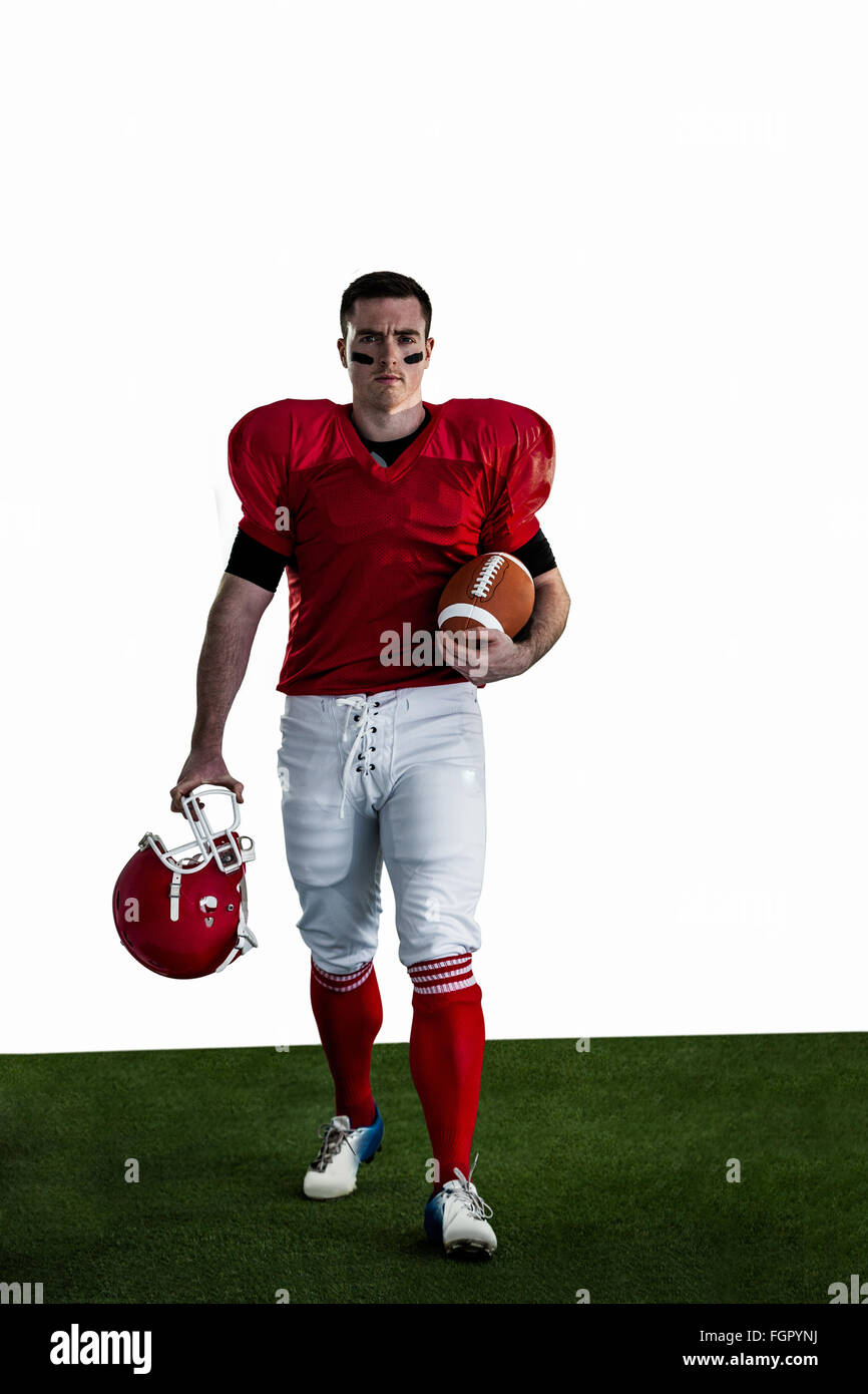 Portrait of american football player walking and holding football and ...