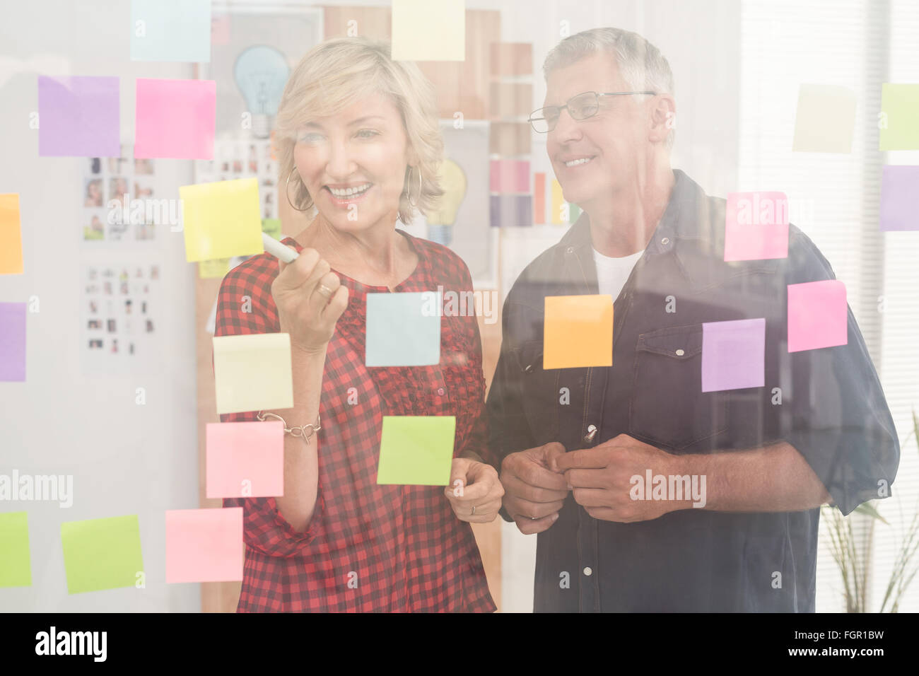 Smiling business team pointing post its on the wall Stock Photo - Alamy