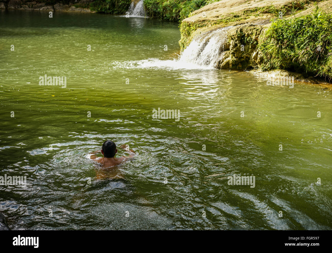 landscape with small waterfall by the lake and a swimming person on a ...