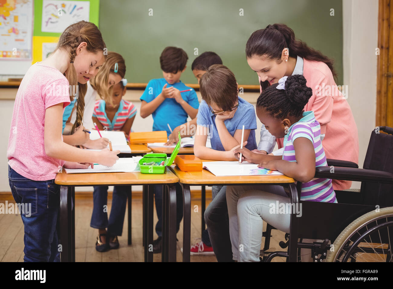 Pupils and teacher working at desk together Stock Photo - Alamy