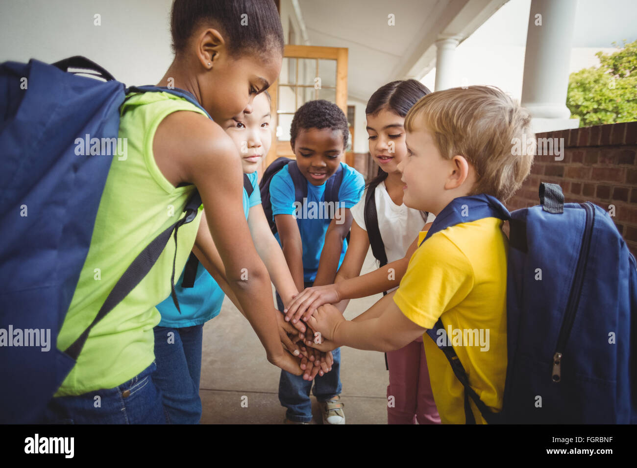 Happy pupils putting hands together at corridor Stock Photo - Alamy
