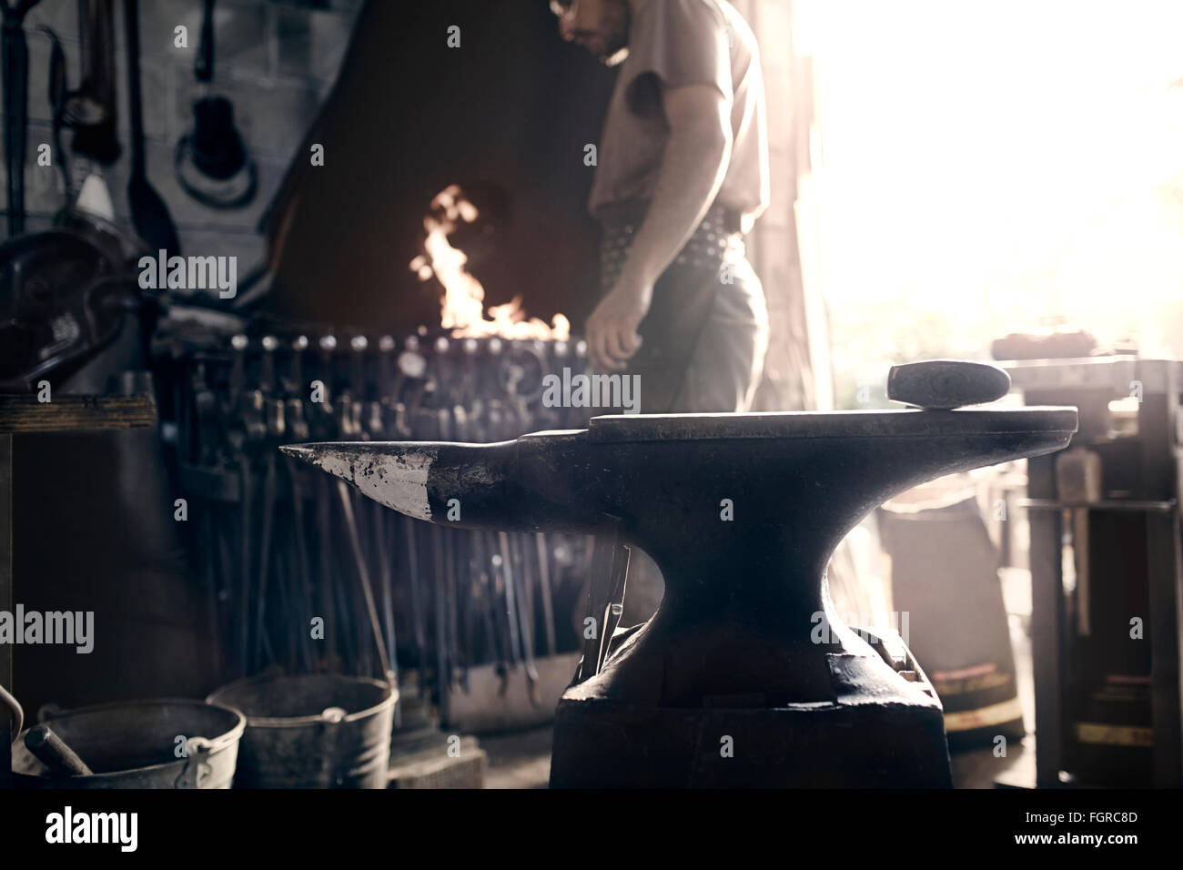 Blacksmith at fire behind anvil in forge Stock Photo - Alamy