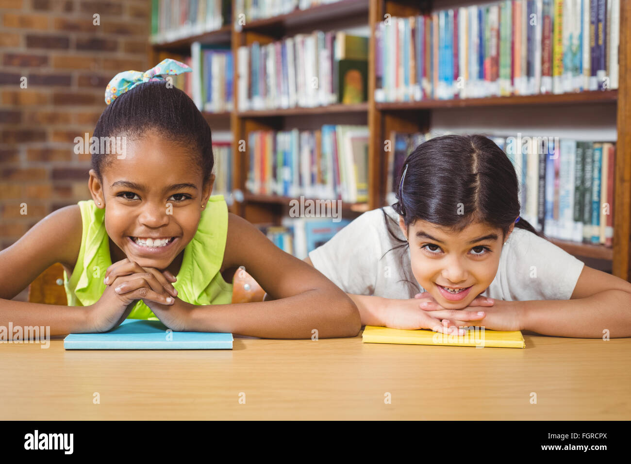 Smiling pupils leaning on books in the library Stock Photo - Alamy
