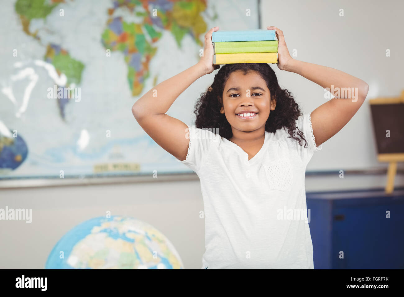 Smiling pupil balancing books on head in a classroom Stock Photo - Alamy