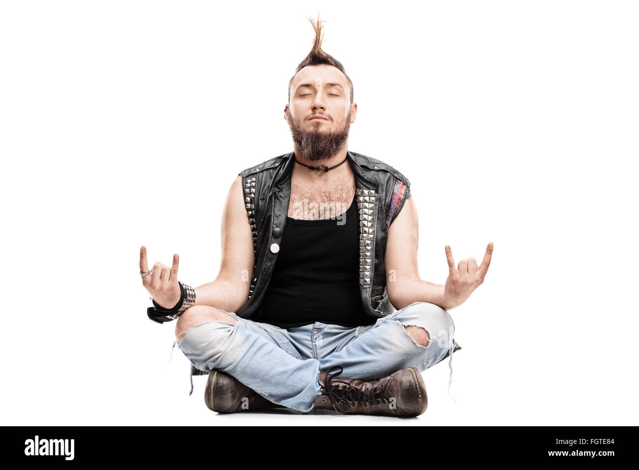 Male punk meditating seated on the floor and making a rock gesture with ...