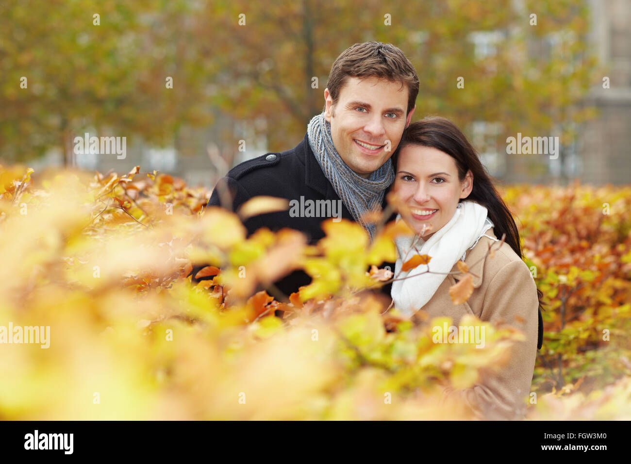 Happy smiling couple behind hedge in a fall park Stock Photo - Alamy