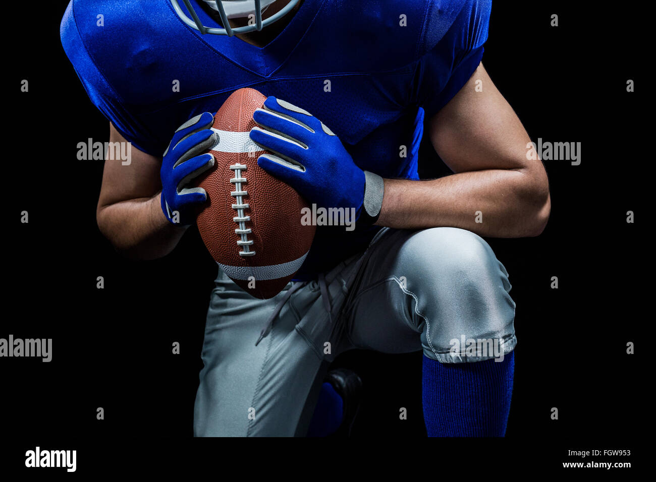 Mid section of American football player kneeling while holding ball ...