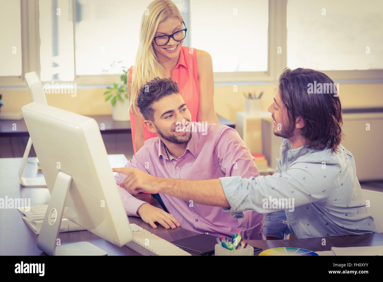 Businessman pointing on computer as smiling colleagues looking at it ...