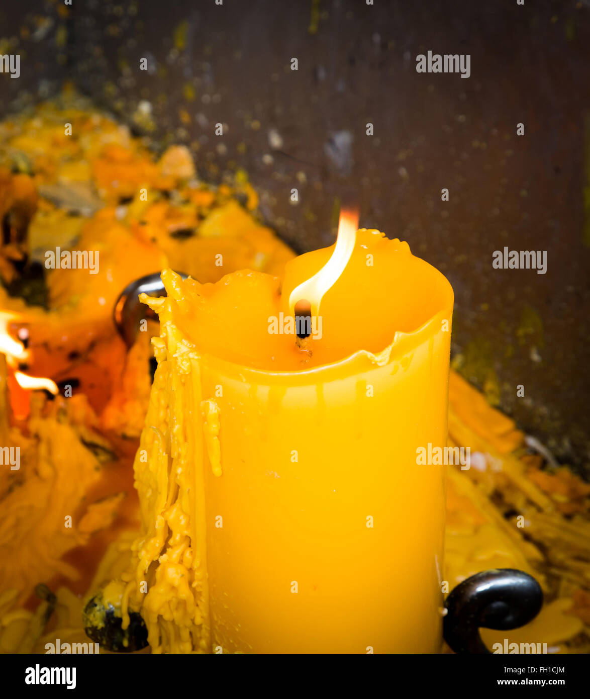 Big yellow candle with fire burn on the top and melt wax beside. It put ...