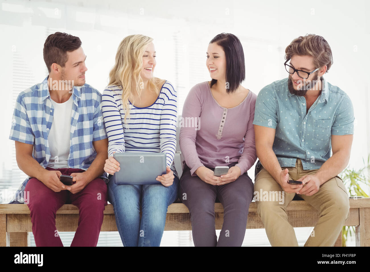 Smiling business people holding electronic gadgets while sitting on ...