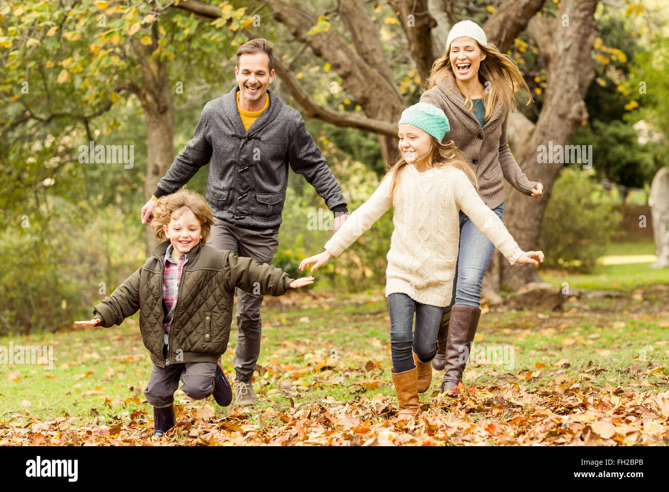 Smiling young family running into leaves Stock Photo - Alamy