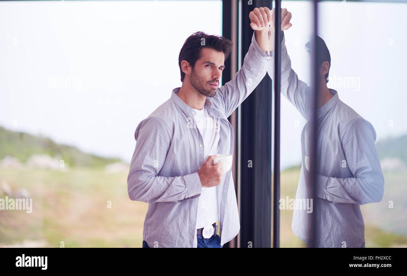 relaxed young man drink first morning coffee withh rain drops on window ...