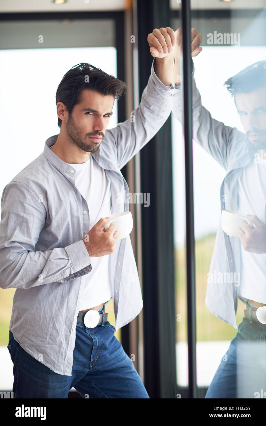 relaxed young man drink first morning coffee withh rain drops on window ...