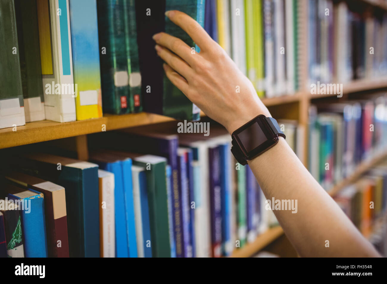 Student picking book in library wearing smart watch Stock Photo - Alamy