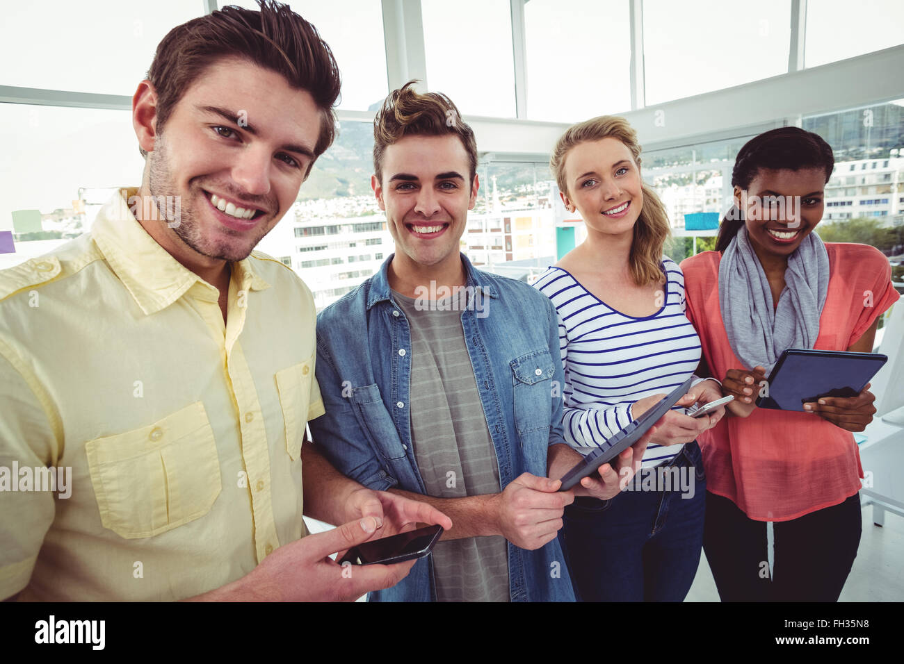 Smiling creative team standing in a line using technology Stock Photo ...