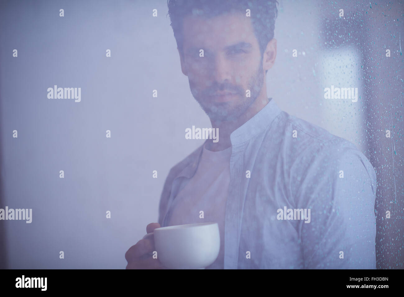relaxed young man drink first morning coffee withh rain drops on window ...