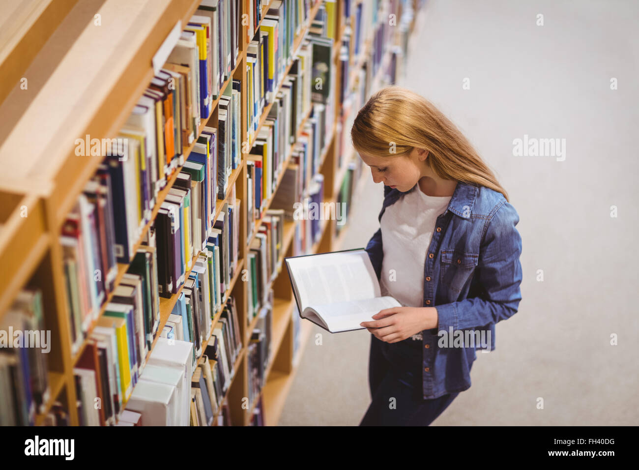 Standing student reading book in library Stock Photo - Alamy