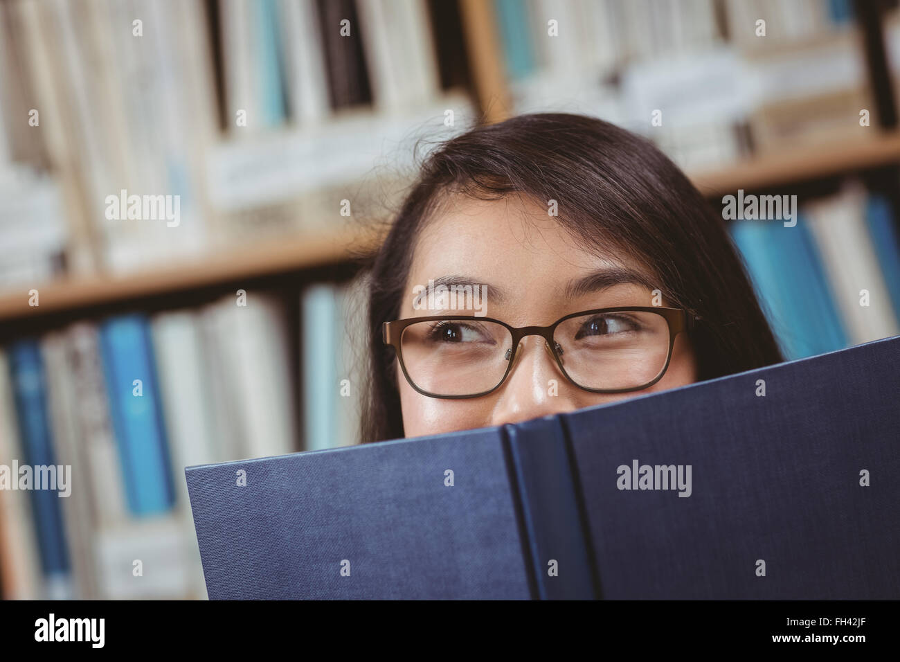 Pretty student hiding face behind a book Stock Photo - Alamy