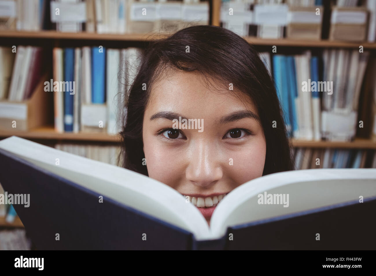 Smiling student hiding face behind a book Stock Photo - Alamy