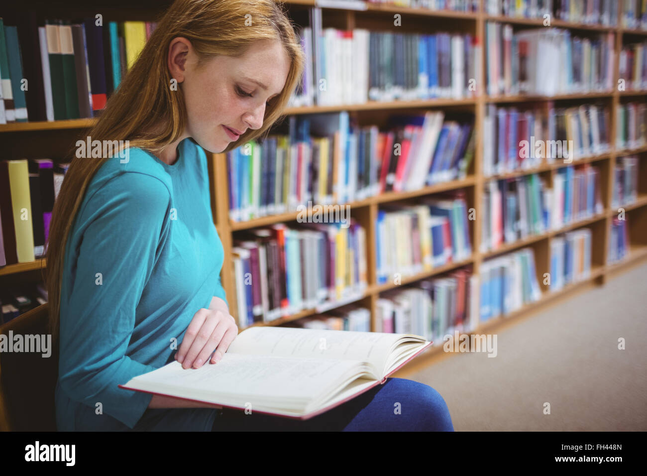 Pretty student sitting on chair reading book in library Stock Photo - Alamy