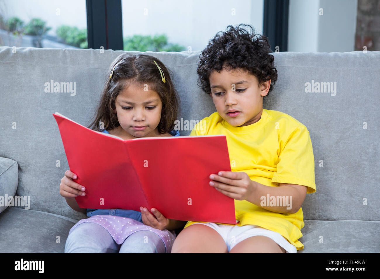 Cute siblings reading a book on the sofa Stock Photo - Alamy