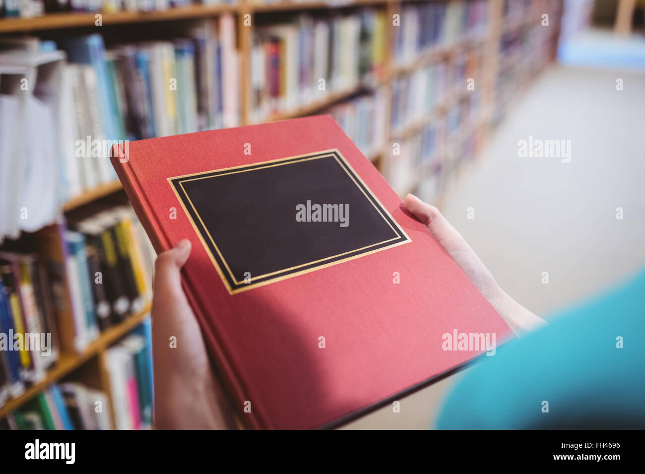 Over shoulder view of student in library holding book Stock Photo - Alamy