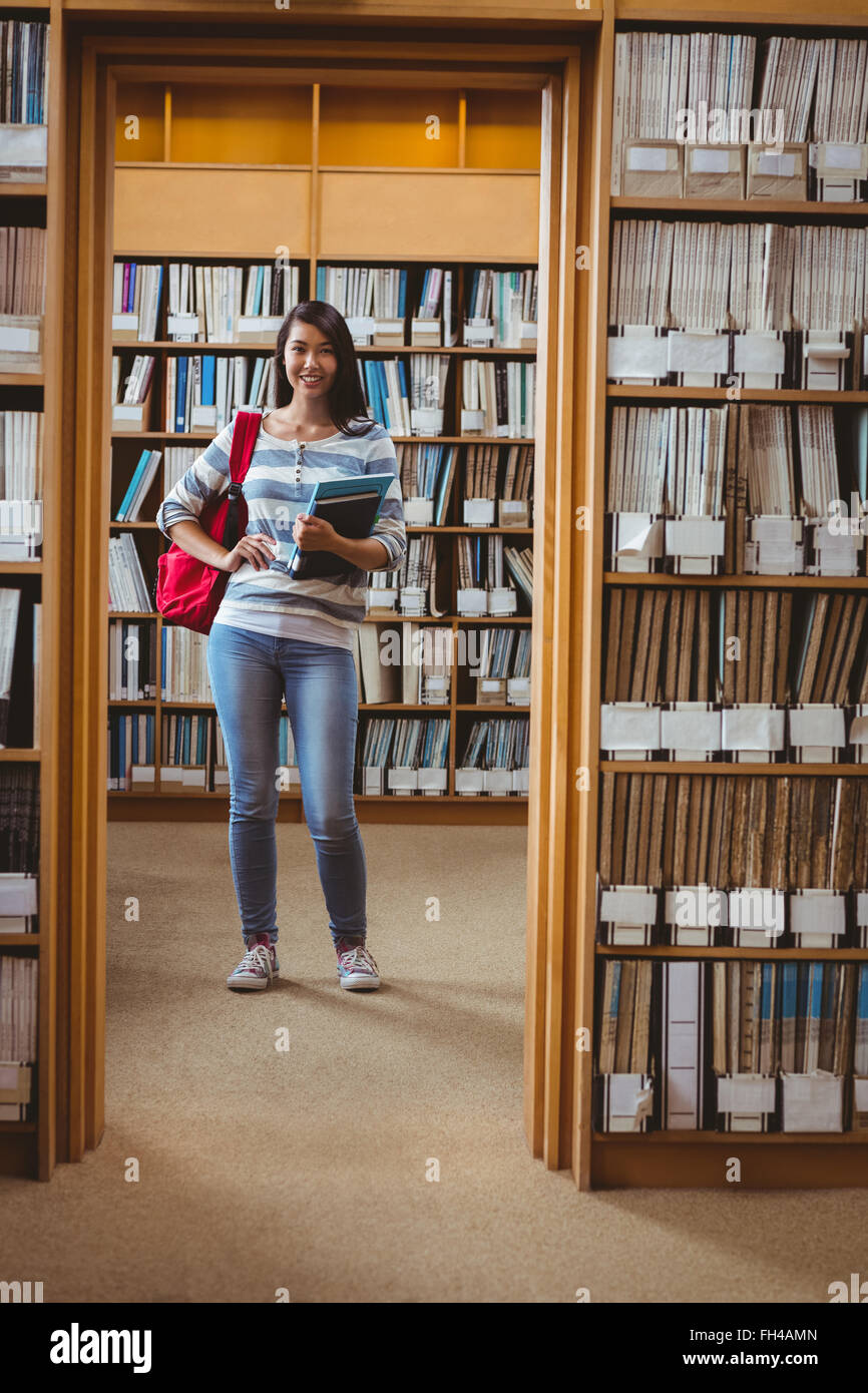 Pretty student standing in library holding a book Stock Photo - Alamy