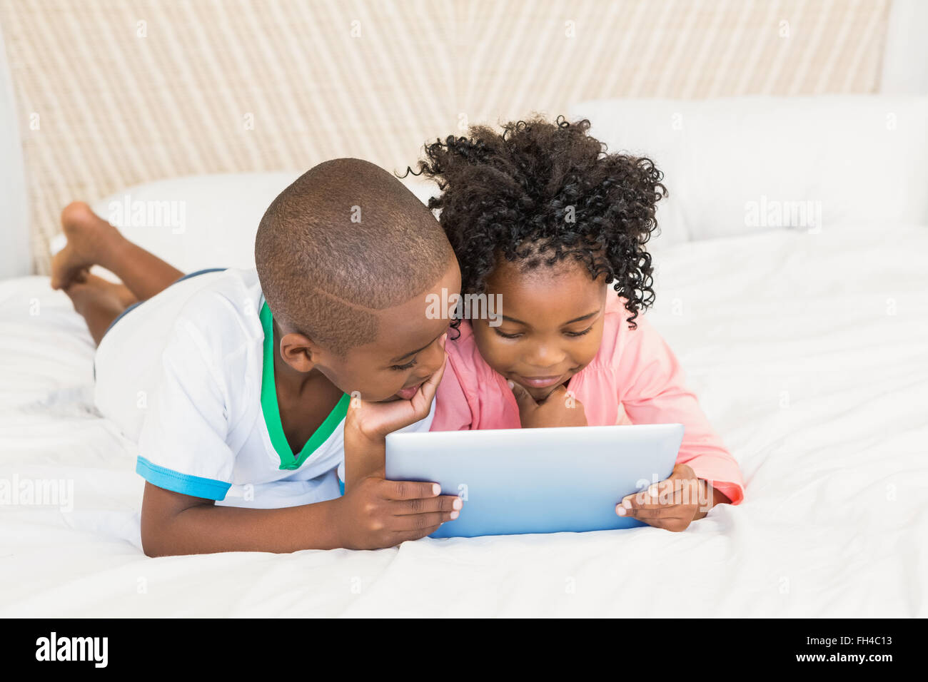 Happy siblings using tablet on bed Stock Photo - Alamy