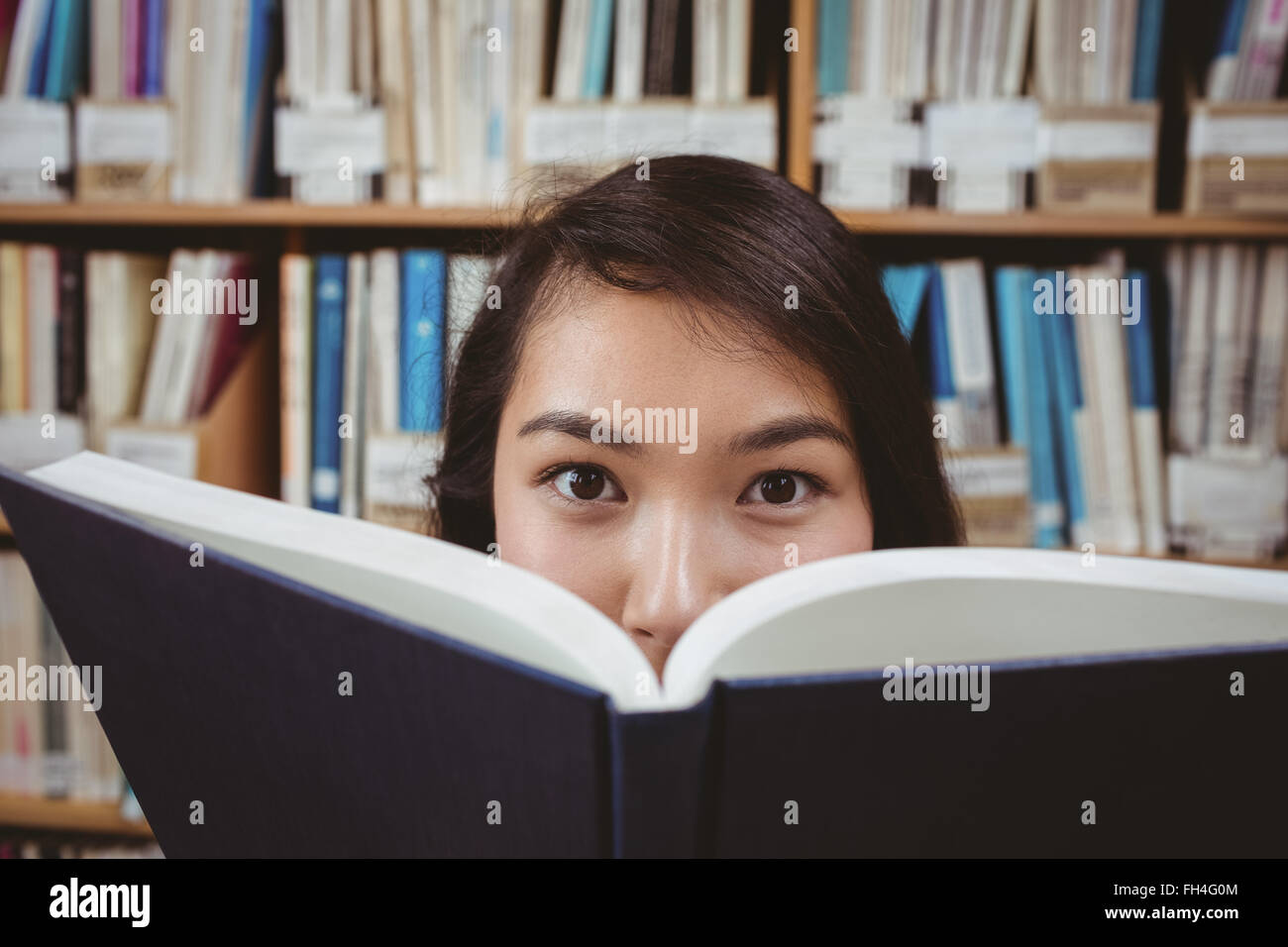 Pretty student hiding face behind a book Stock Photo - Alamy