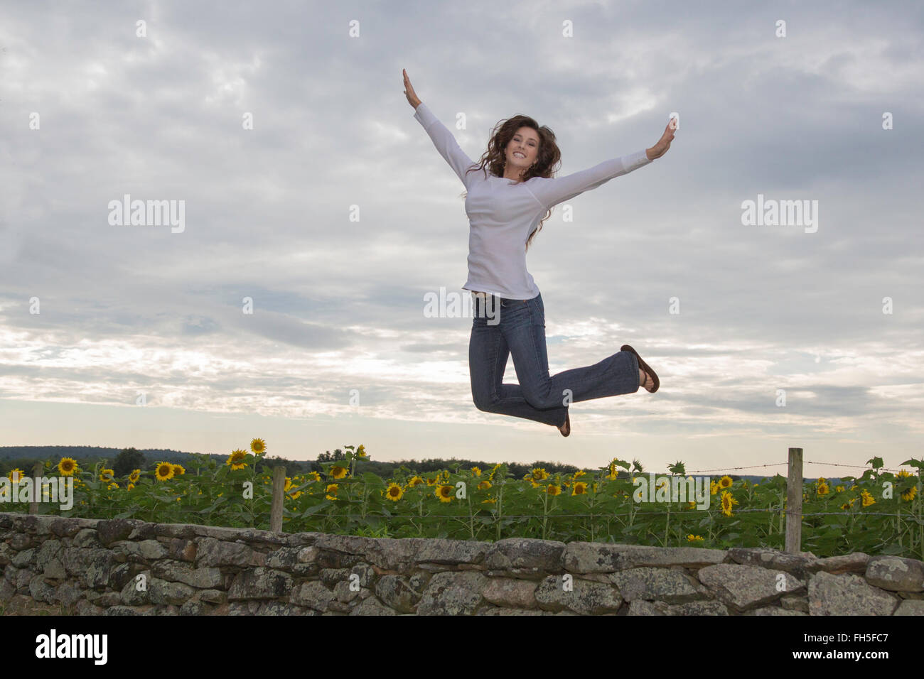 Beautiful brunette woman jumping off a stone wall with sunflowers in ...