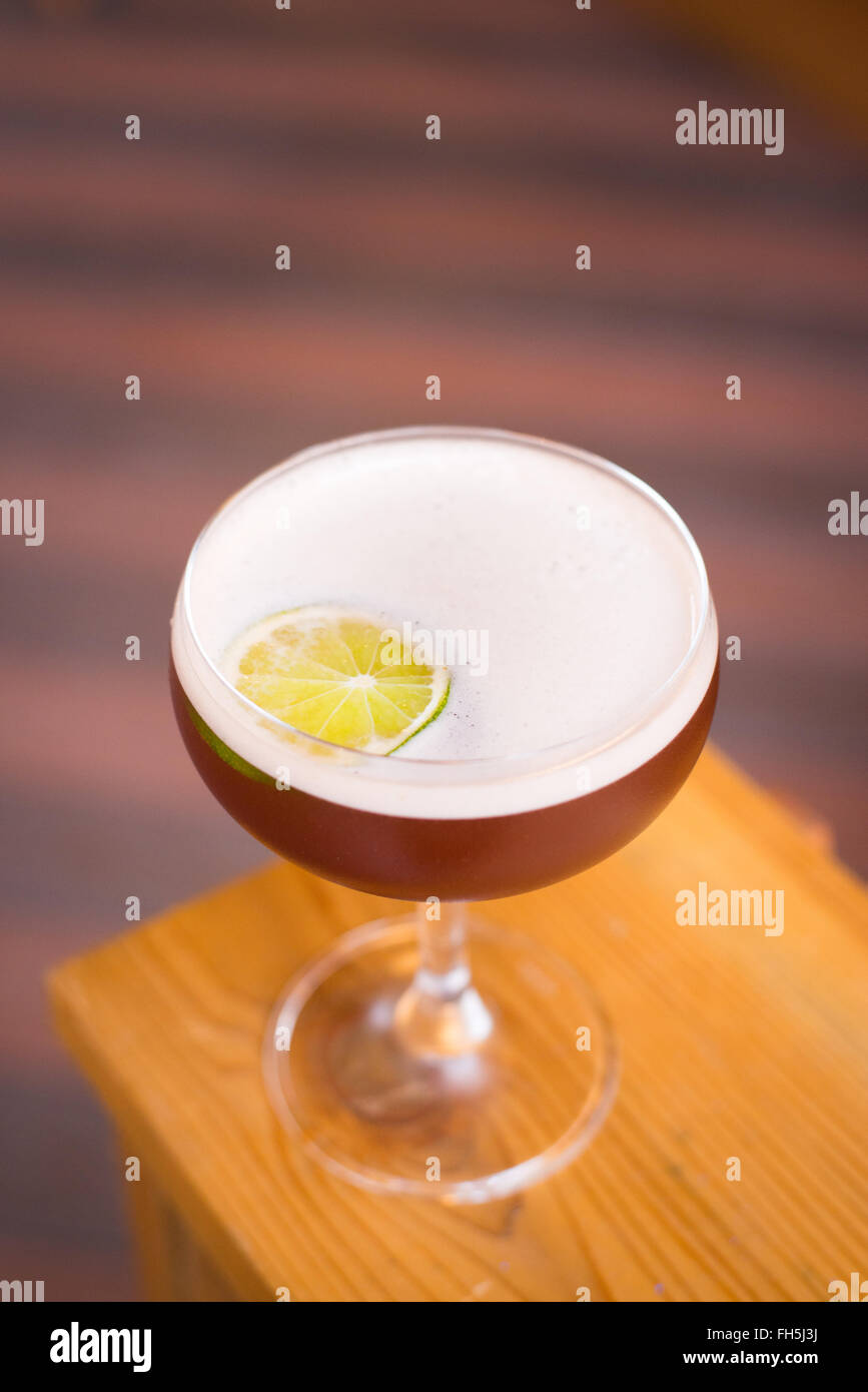 A softly focused, burgundy-colored cocktail with a lime garnish in a ...