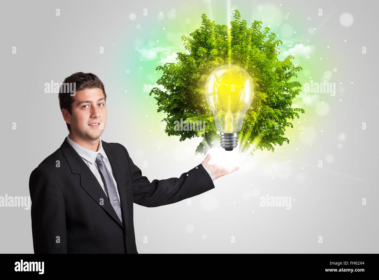 Young man presenting idea light bulb with green tree Stock Photo - Alamy