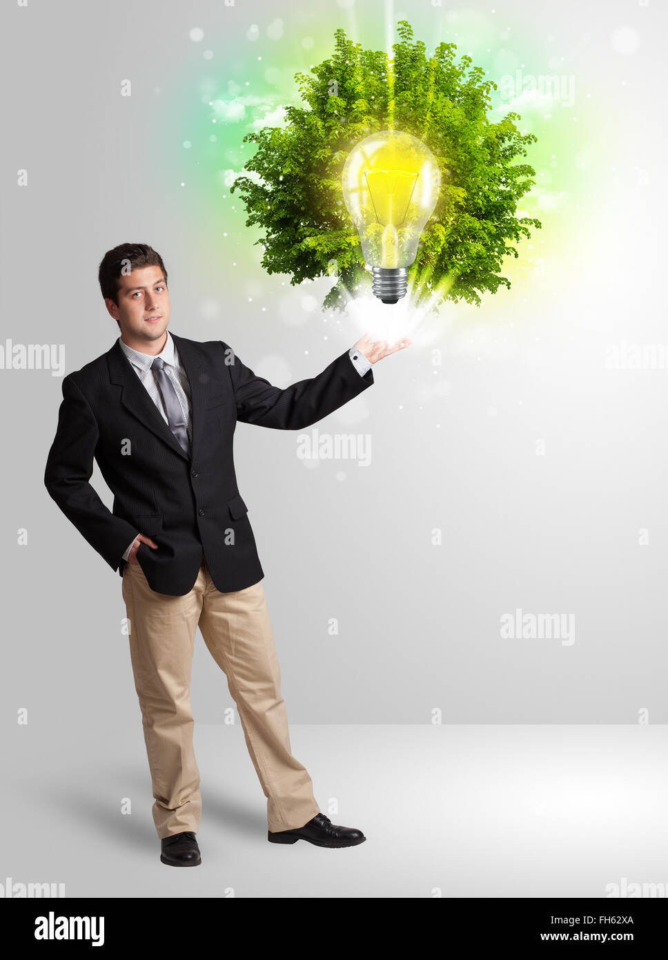 Young man presenting idea light bulb with green tree Stock Photo - Alamy