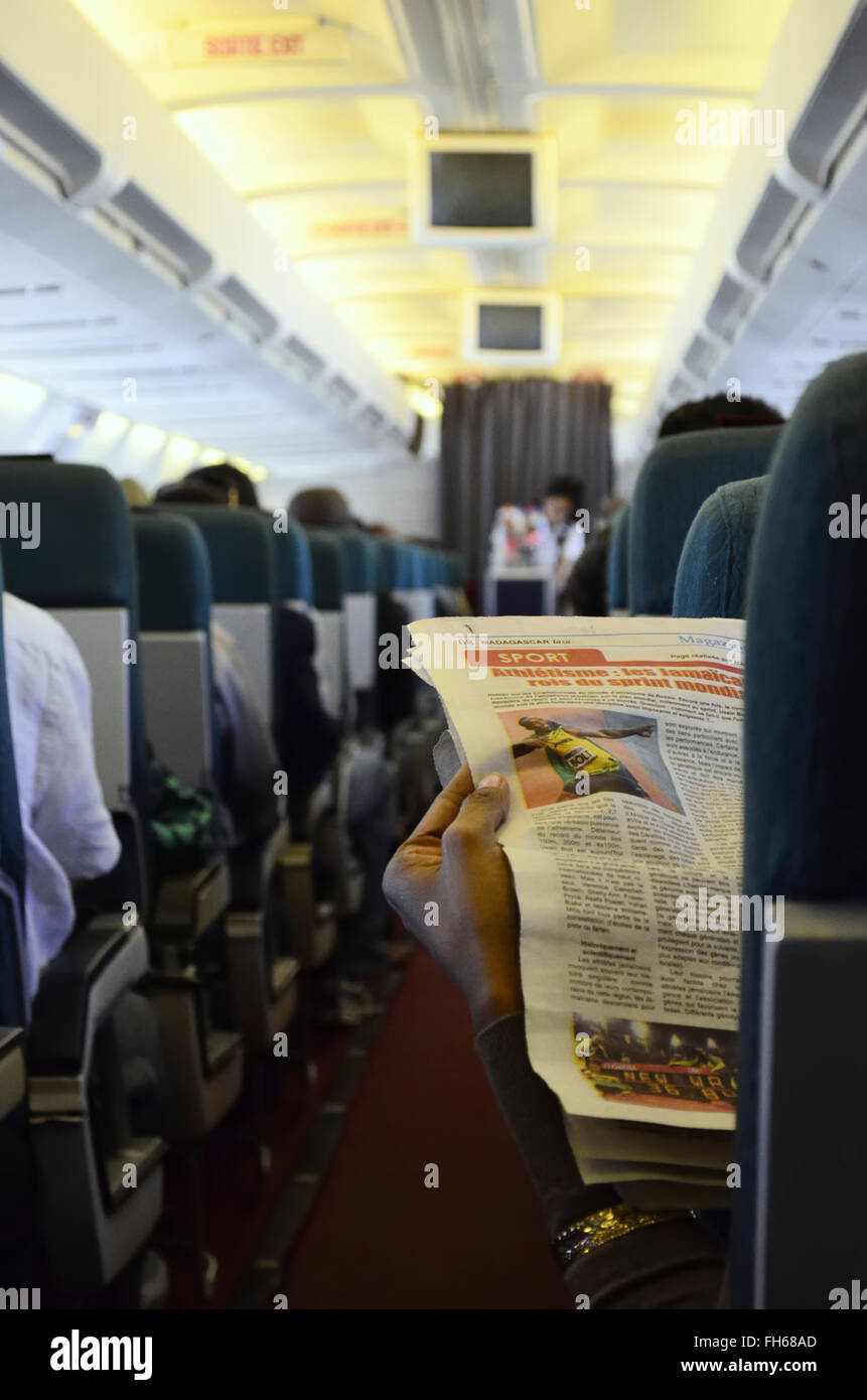 A person reading a newspaper in an airplane or Air Madagascar Stock ...
