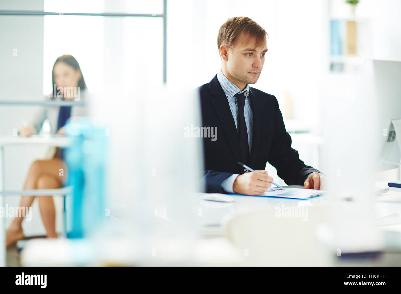 Serious young businessman looking at computer monitor and checking data ...