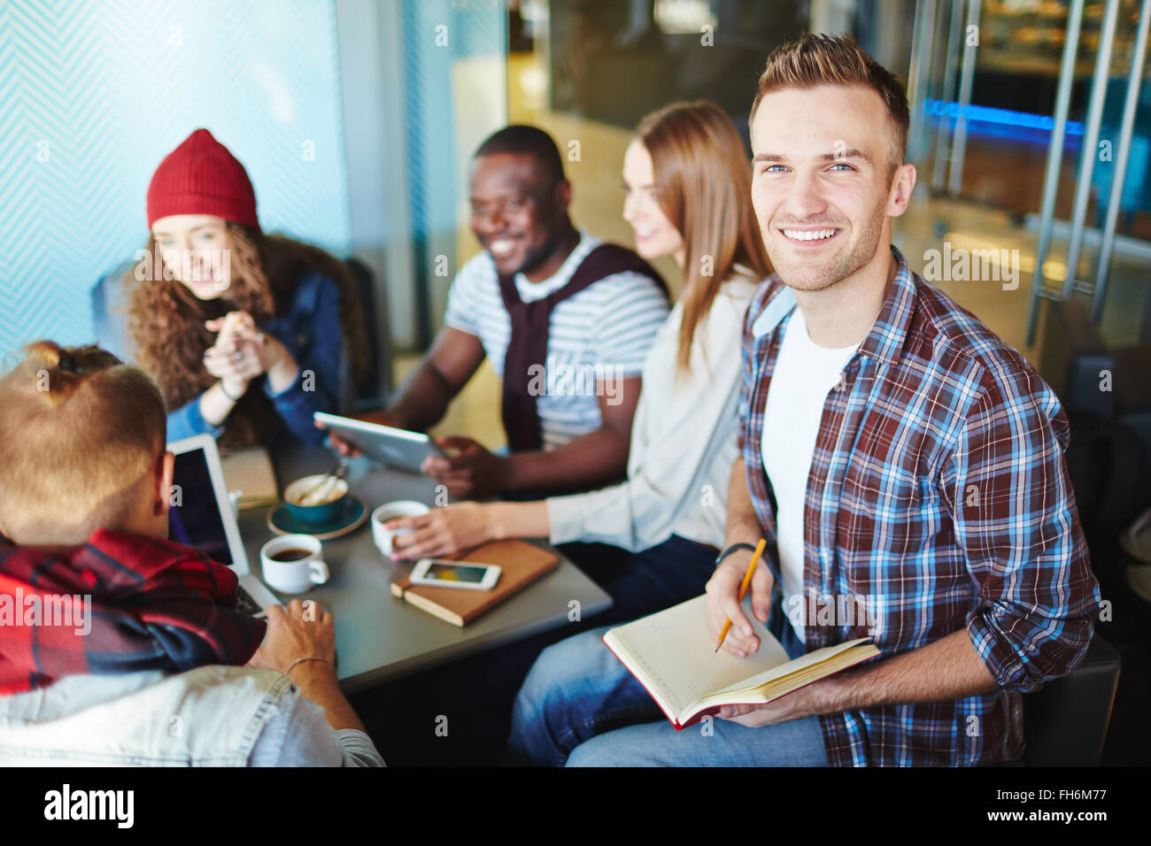 Smiling guy with notepad looking at camera in cafe with his friends on ...