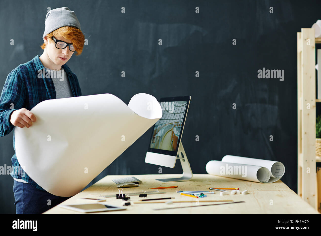 Young serious architect looking at blueprint by workplace Stock Photo ...