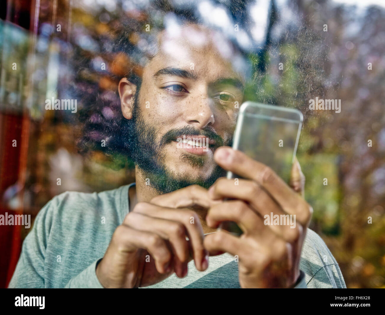 Young man using cell phone behind windowpane Stock Photo - Alamy
