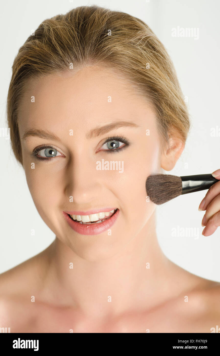 Beautiful young woman applying blusher to her face Stock Photo - Alamy