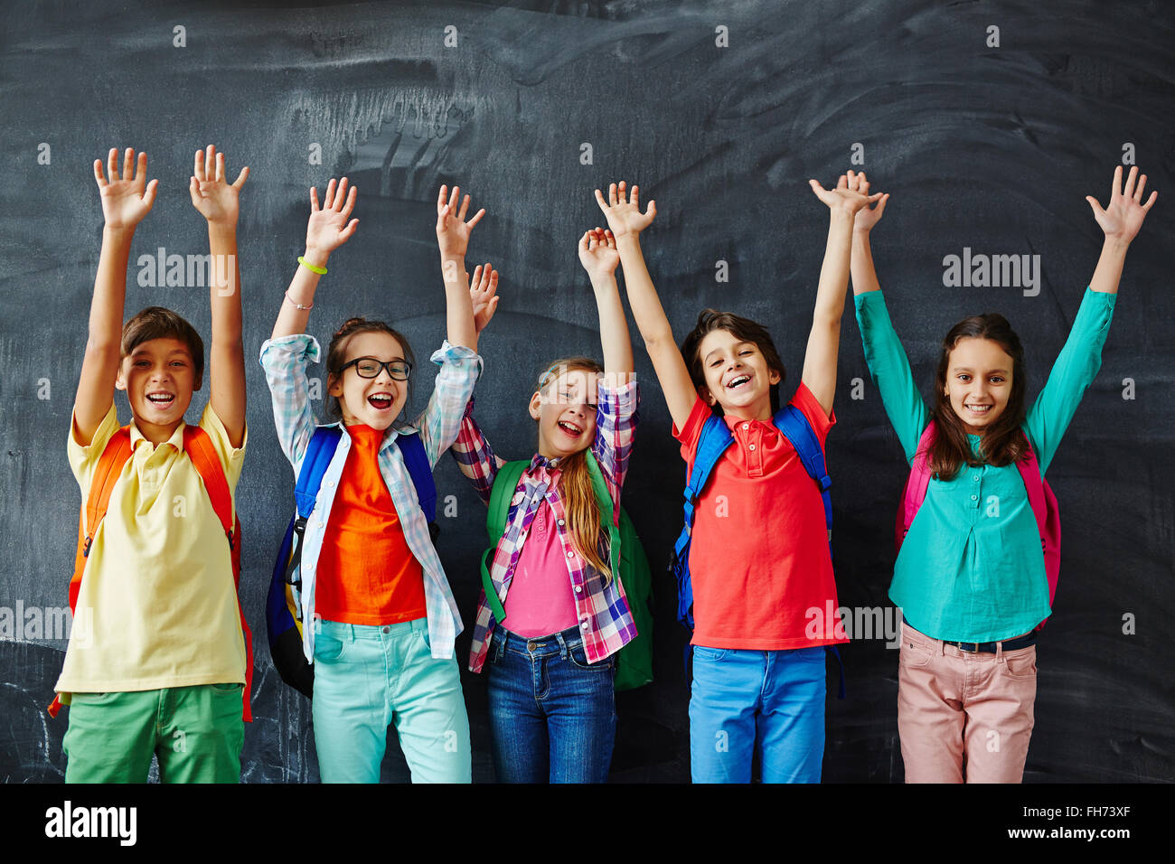 Ecstatic kids raising hands while standing by blackboard Stock Photo ...