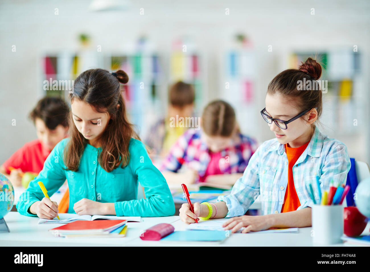Diligent pupils sitting by desk and writing in copybooks at lesson ...