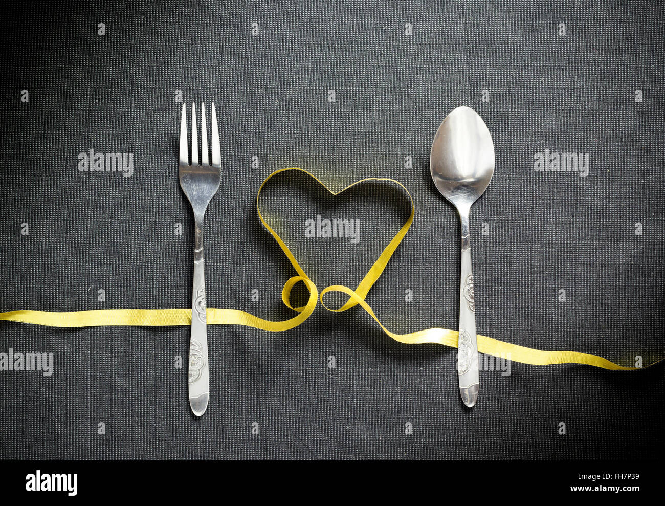 Fork and spoon with heart shape made from yellow ribbon on black ...