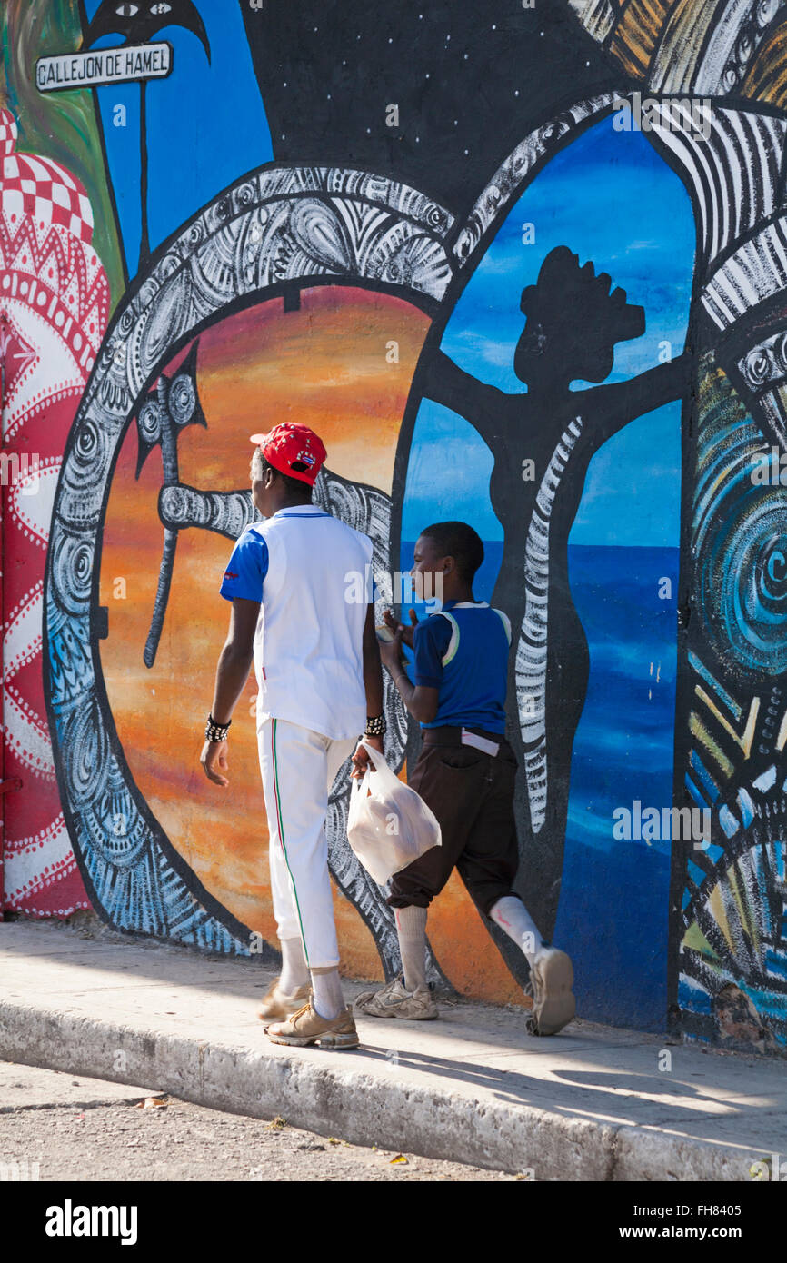 Two Cuban lads walking past Cuban artwork painted on wall at Callejon ...