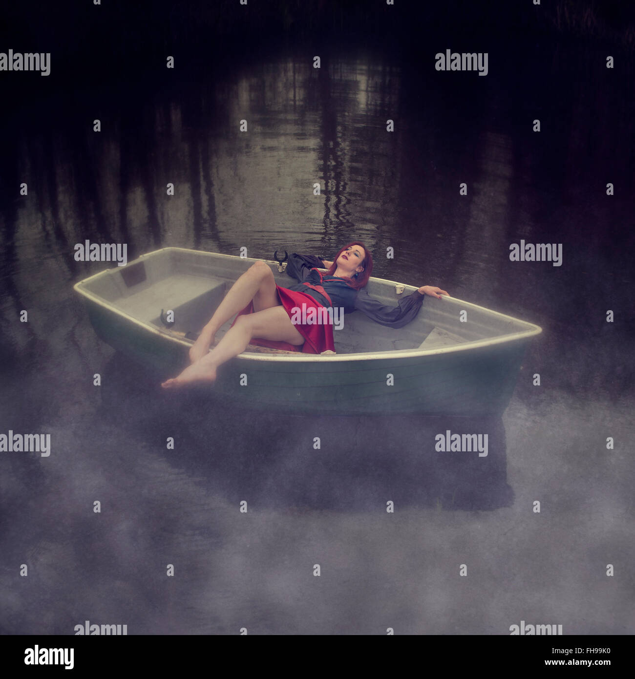 Red haired young woman drifting in a rowing boat, with long bare legs ...